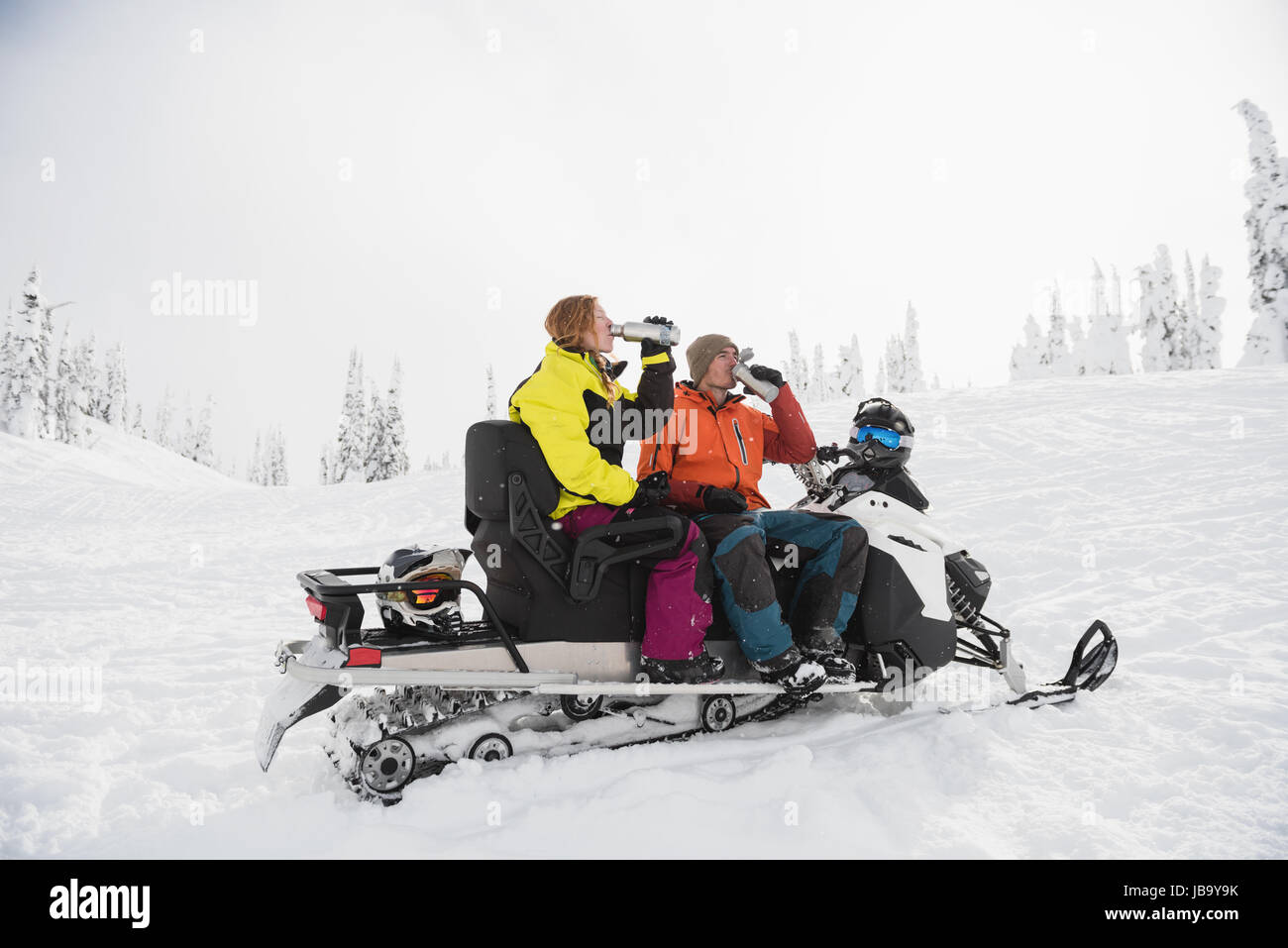 Couple having coffee from thermos while relaxing on snowmobile during ...