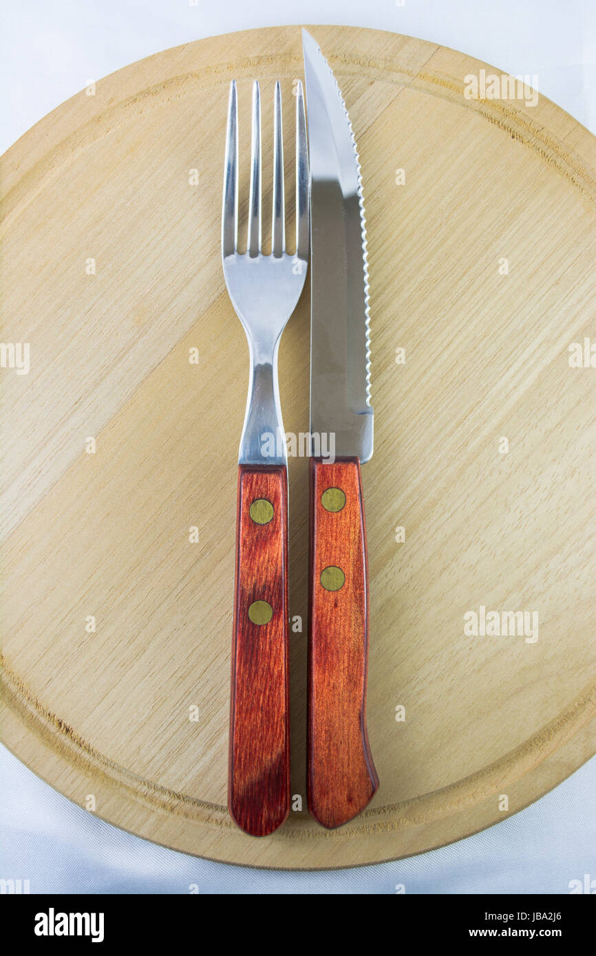 Fork and knife with red wooden handle on a plate of natural wood Stock ...
