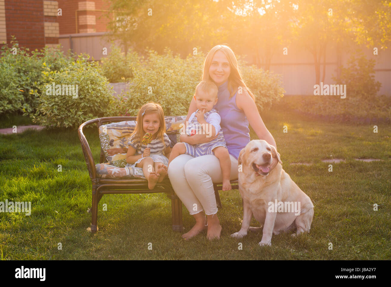 Happy mother and two children with Golden Retriever dog in the garden ...
