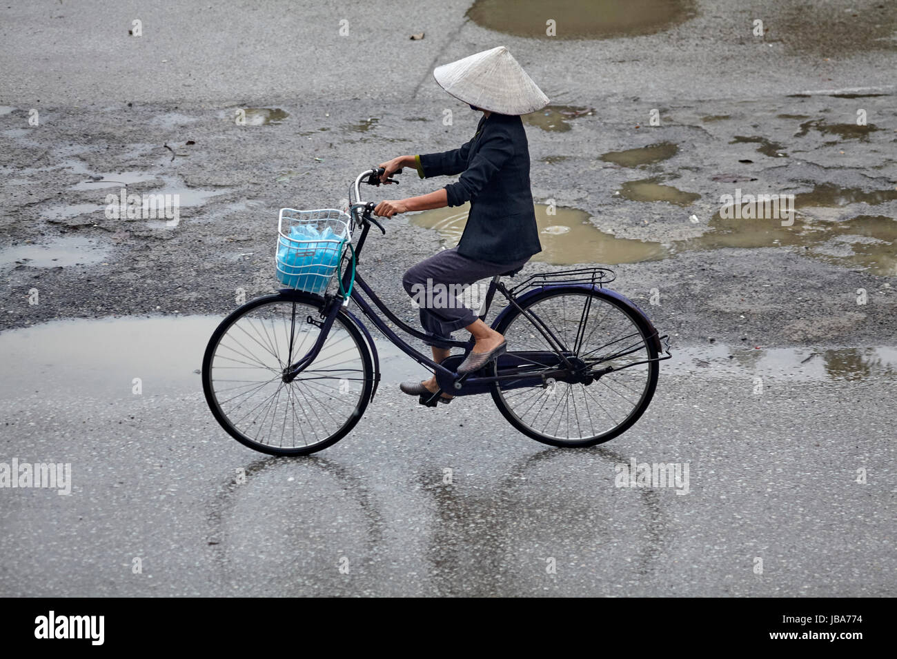 Woman in conical hat cycling in the rain, Ninh Binh, Vietnam Stock ...