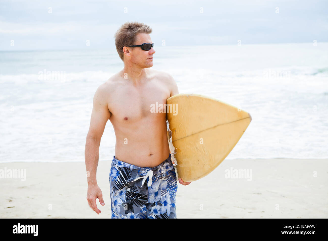 Relaxed and focused looking male surfer walking on beach while carrying ...