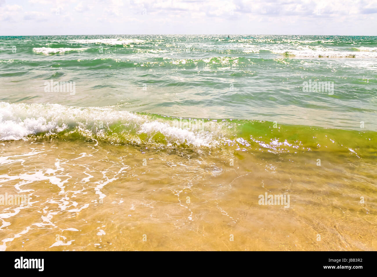 Beautiful green ocean with a wave hitting the sandy beach Stock Photo ...