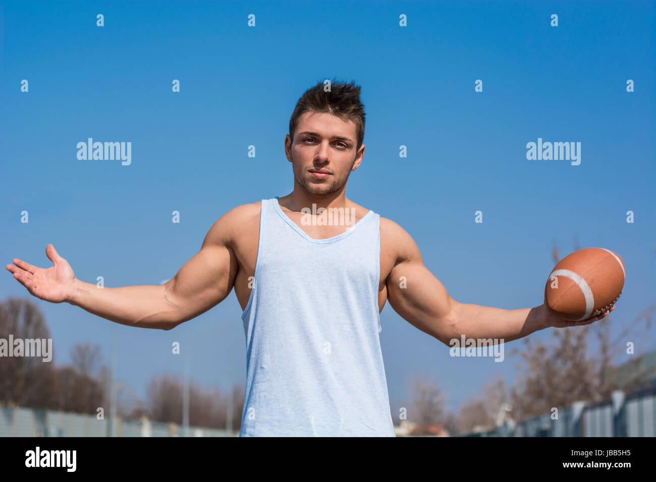 Muscular american football player standing with ball in hand, arms open ...