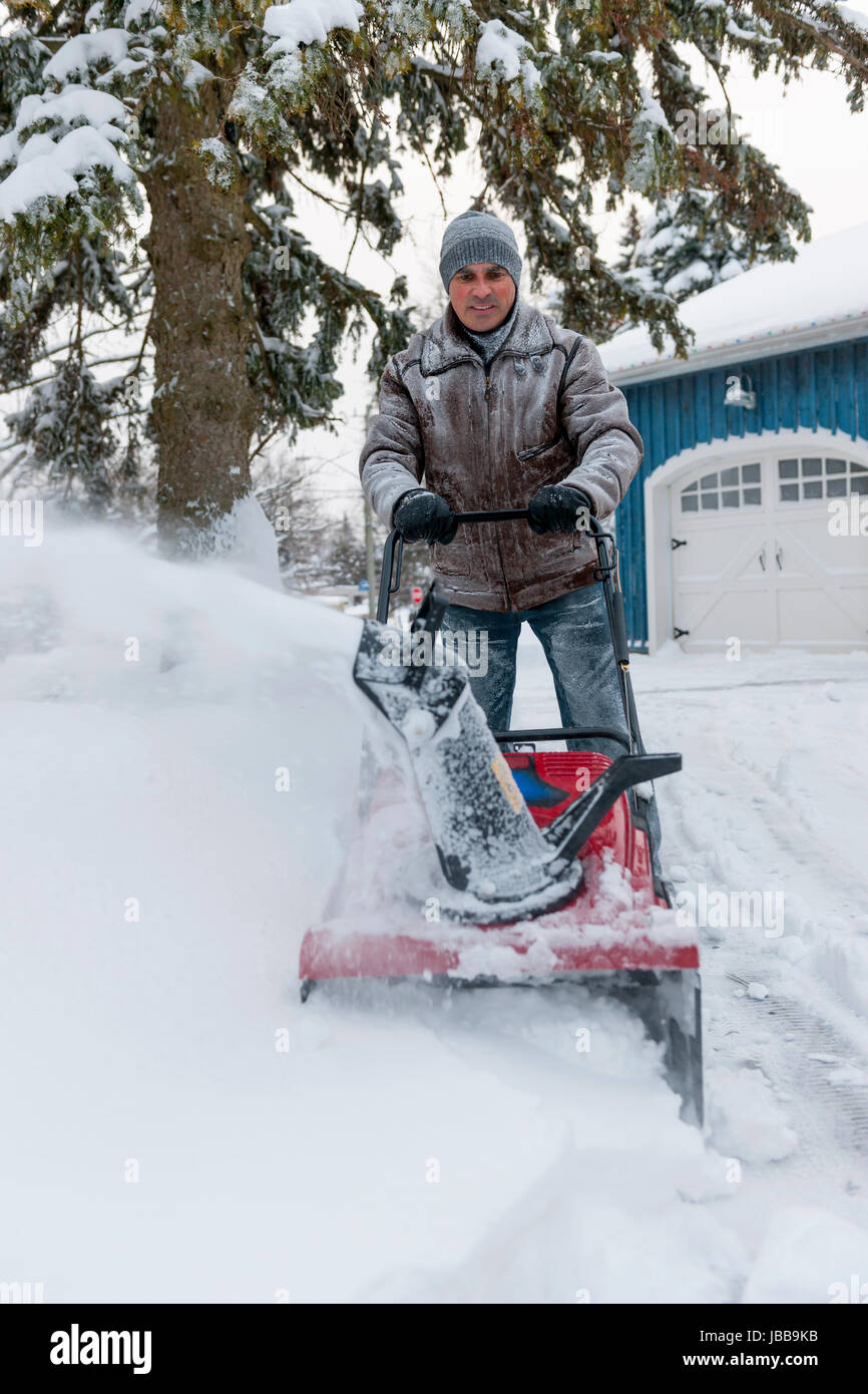 Man using snowblower to clear deep snow on driveway near residential ...