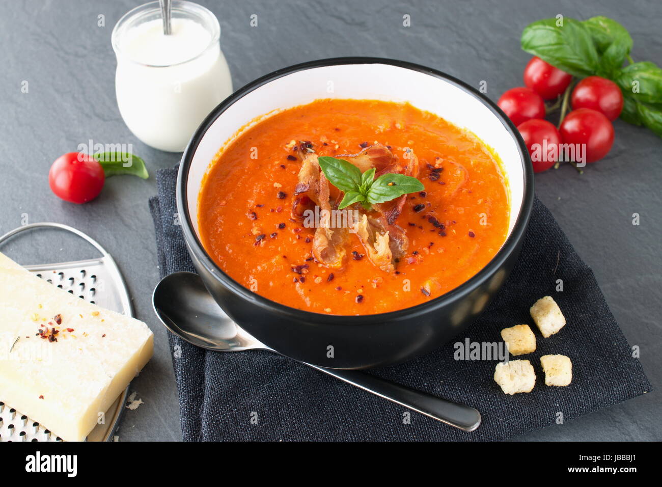 Thick tomato soup with basil and fried bacon in a black ceramic bowl on ...