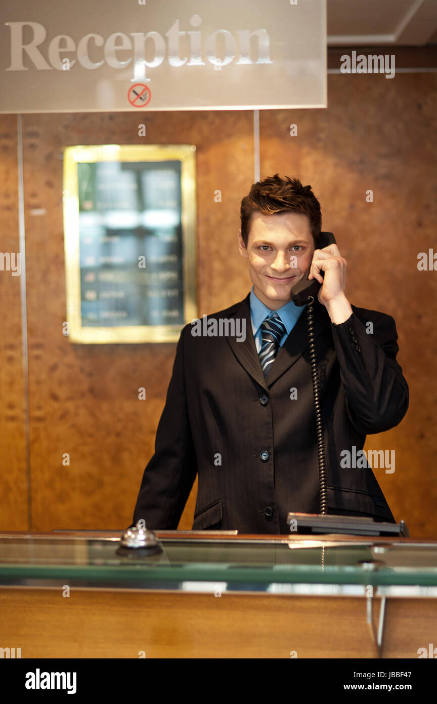 Profile shot of a handsome receptionist on the phone posing in front of ...