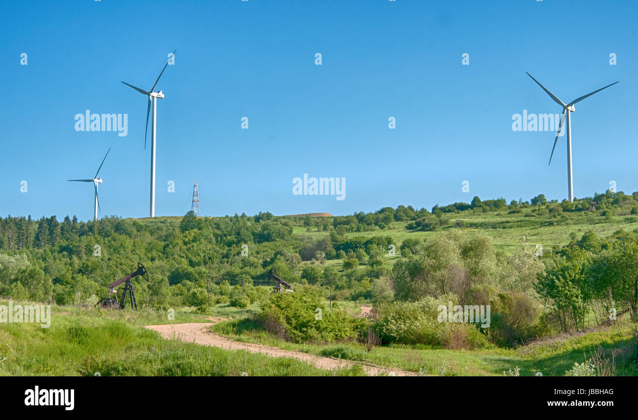 New energy era is coming. An old oil pump jack in front of modern wind ...