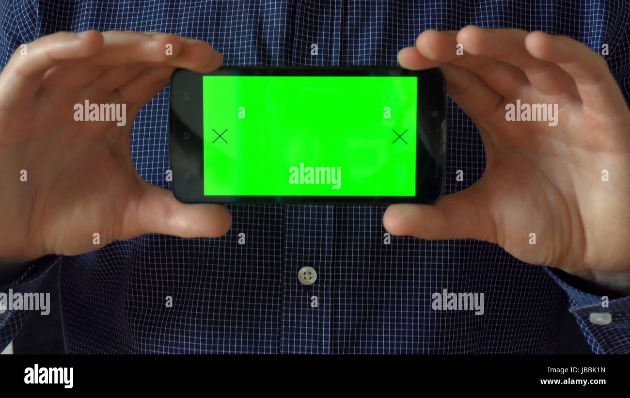 young man in shirt holding phone with green screen in front of him ...