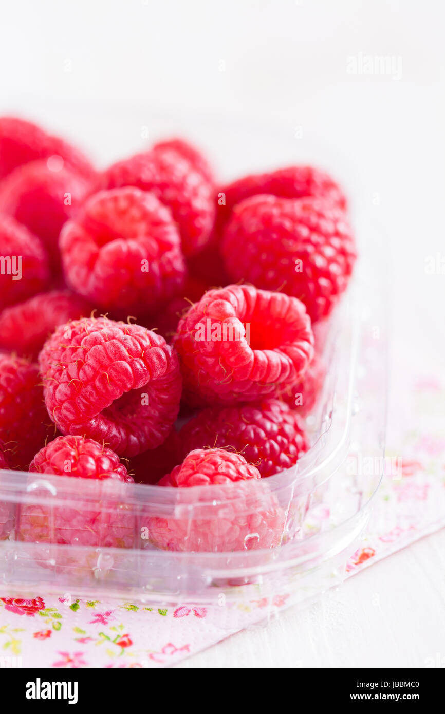 Closeup of bunch of fresh red raspberries in clear plastic container ...