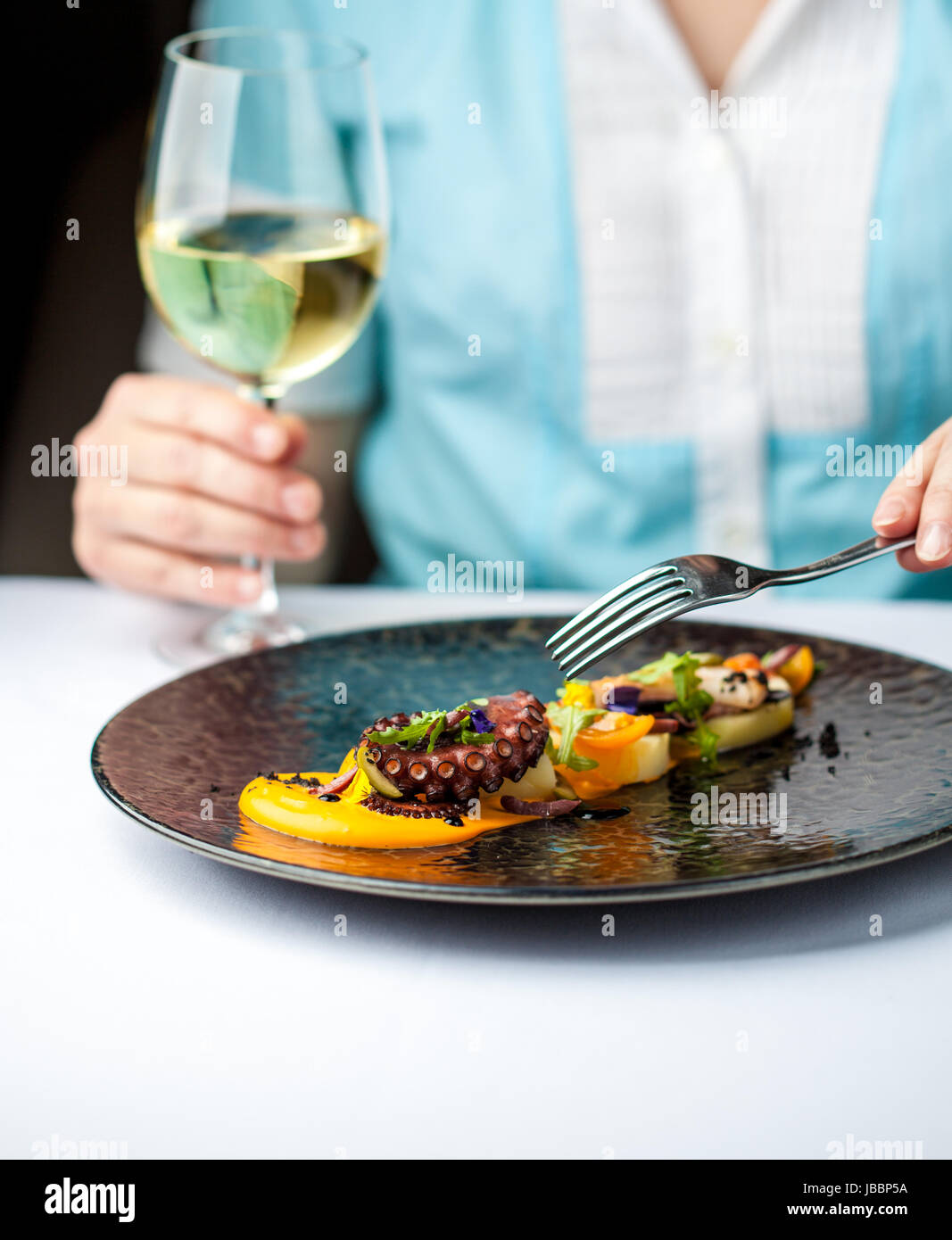 Woman is eating an octopus and drinking wine in a restaurant ...