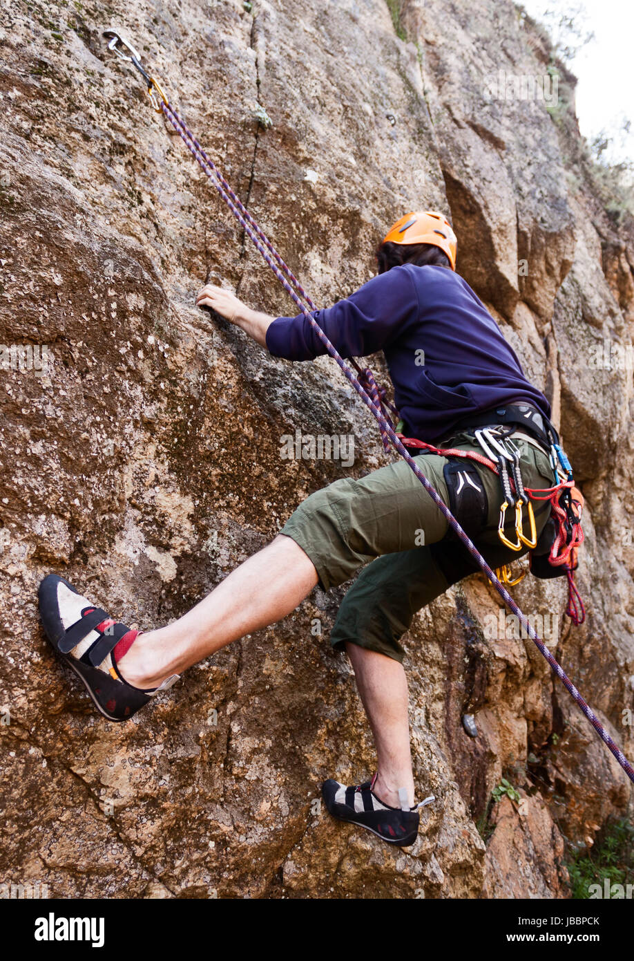 A young man with helmet and rope climbing safely a rock wall outdoors ...