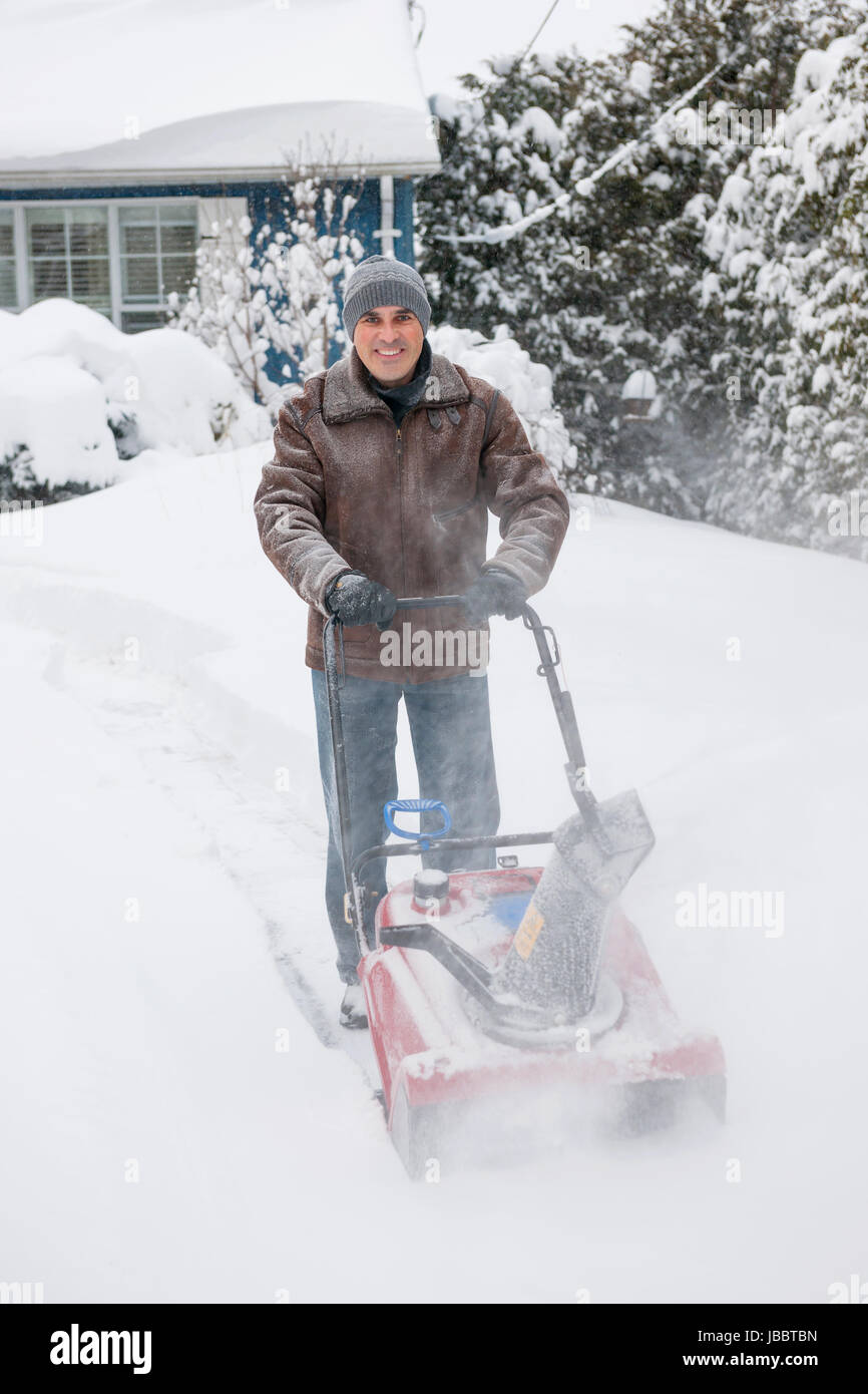 Man using snowblower to clear deep snow on driveway near residential ...