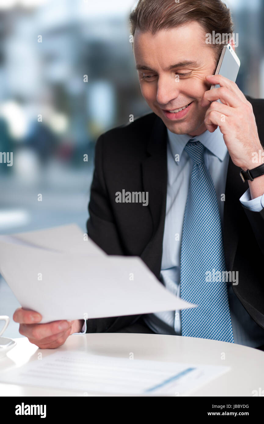 Positive corporate guy communicating on phone with reports in hand ...