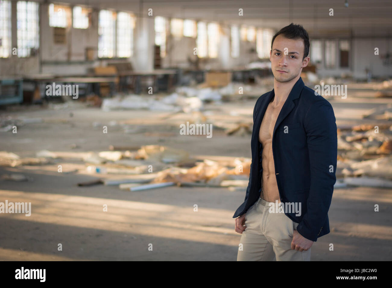 Muscular young man with jacket on naked torso in empty abandoned ...