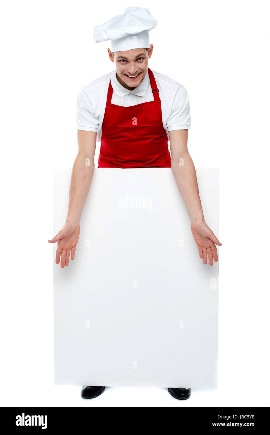 Handsome young cook showing blank billboard against white. Cheerful ...