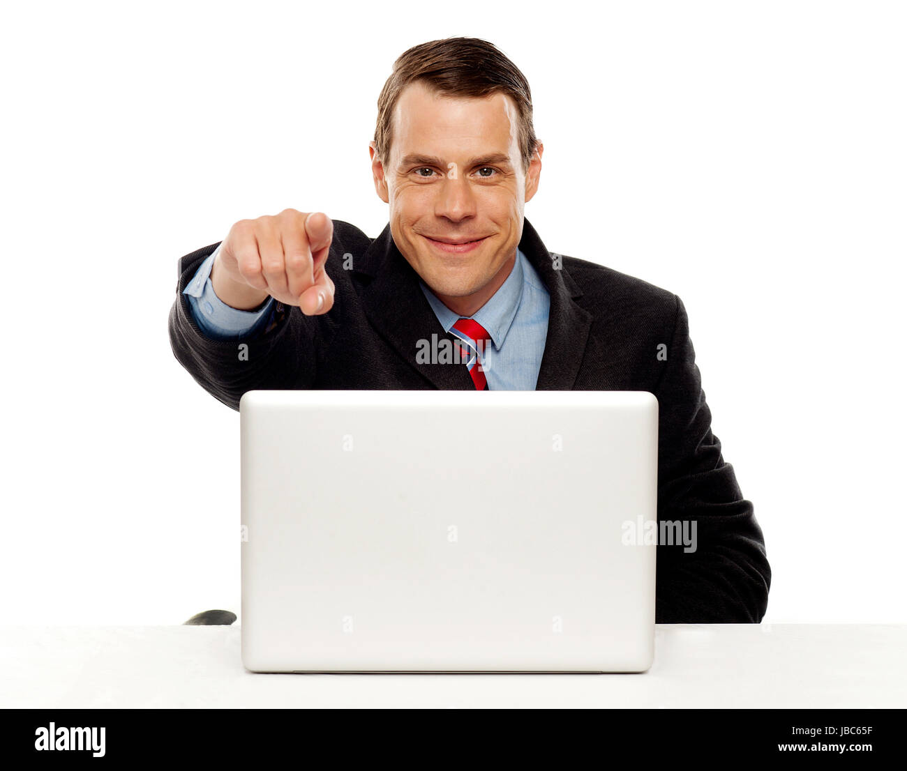 Handsome male executive pointing at you while working on laptop at his ...