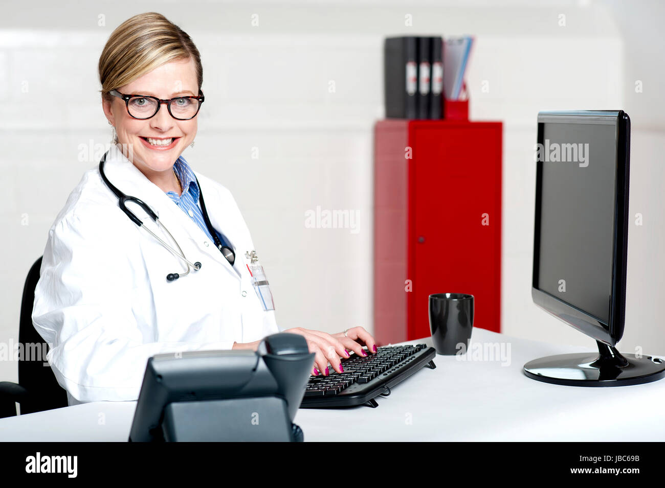 Female physician using computer and smiling at camera Stock Photo - Alamy