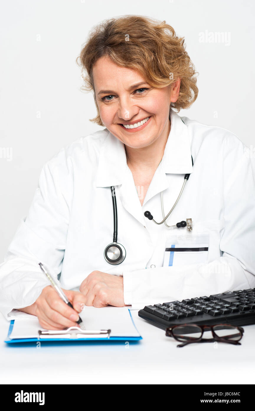 Happy female physician writing prescription seated at work desk Stock ...