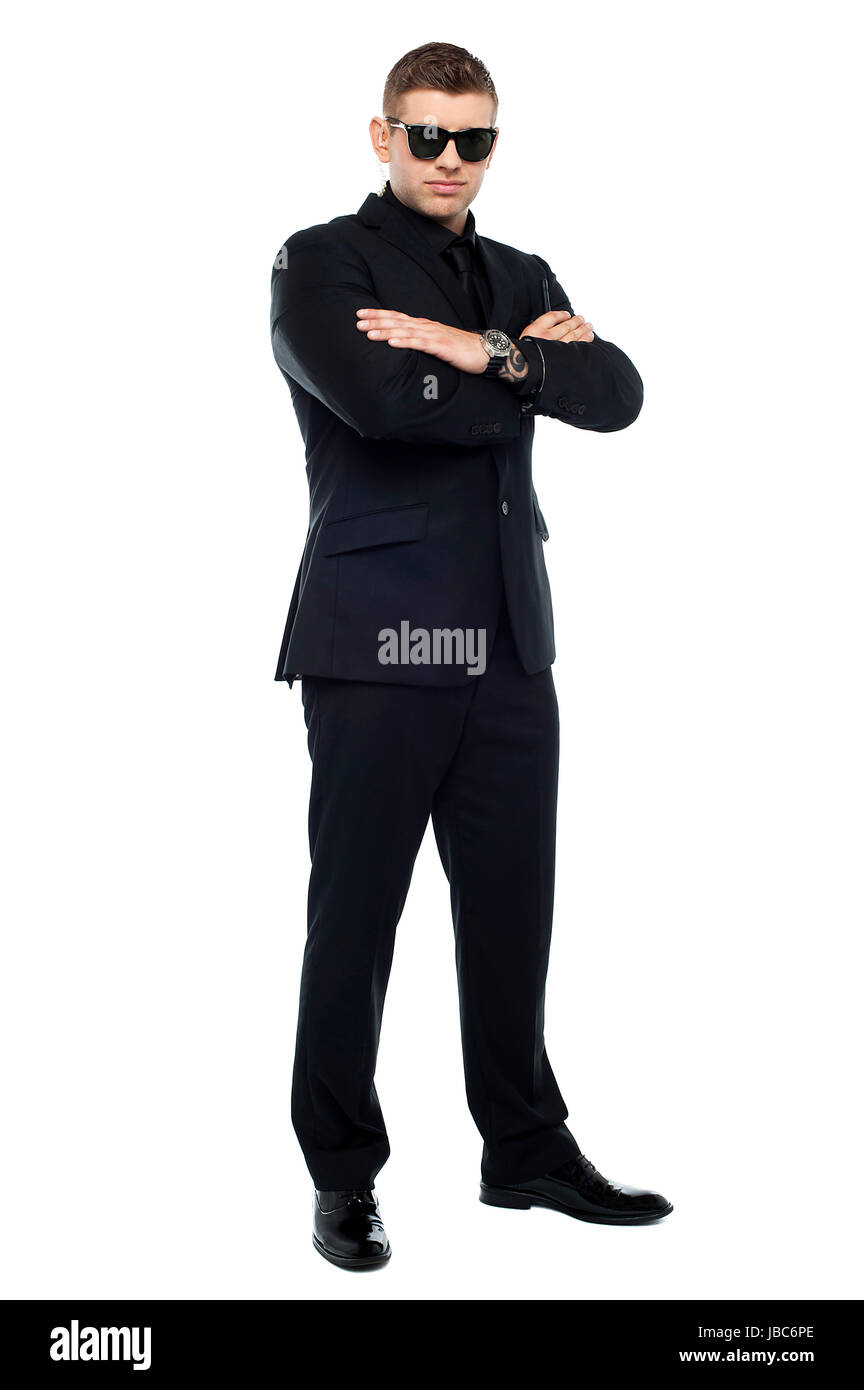 Young stylish bouncer in a black suit, arms folded and wearing goggles ...