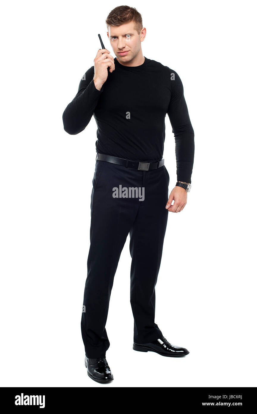 Full length portrait of male bodyguard communicating via walkie-talkie ...