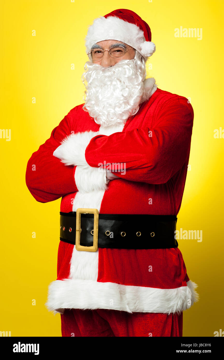 Confident male Santa posing with arms folded isolated over yellow ...