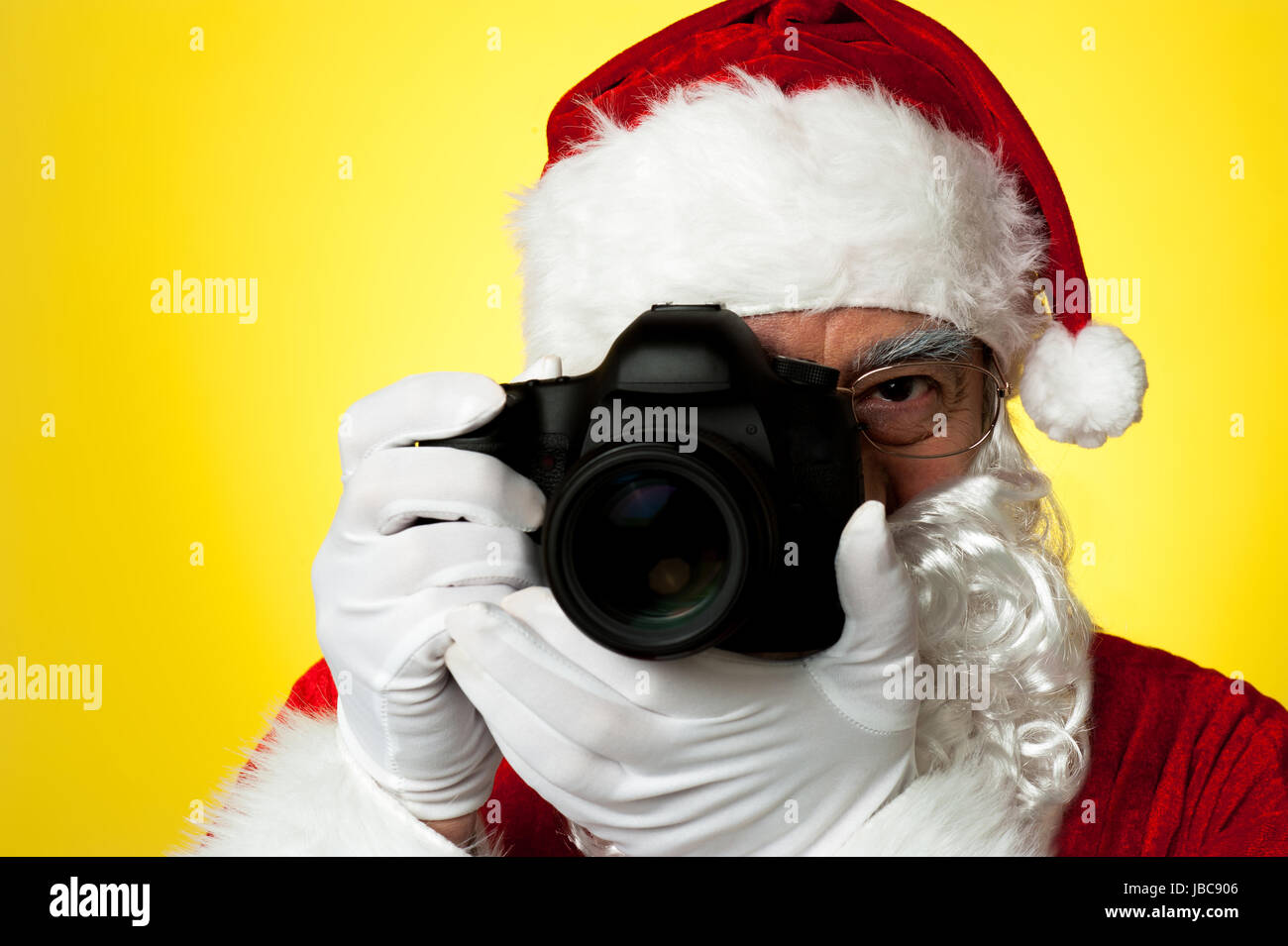 Aged Santa adjusting camera lens before click. Isolated against yellow ...