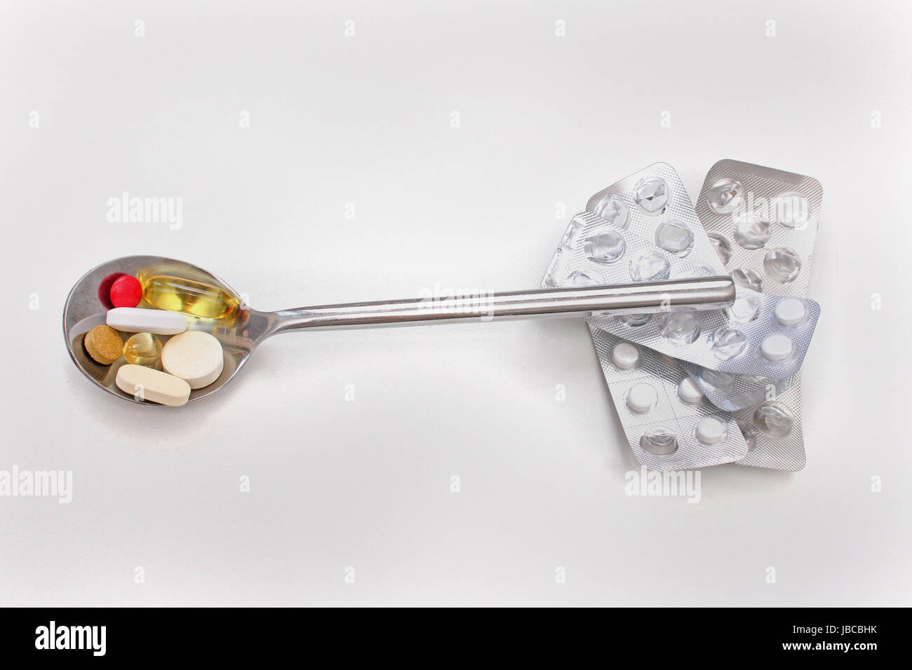 Silver spoon full with colorful pills on top of used tablet blisters ...