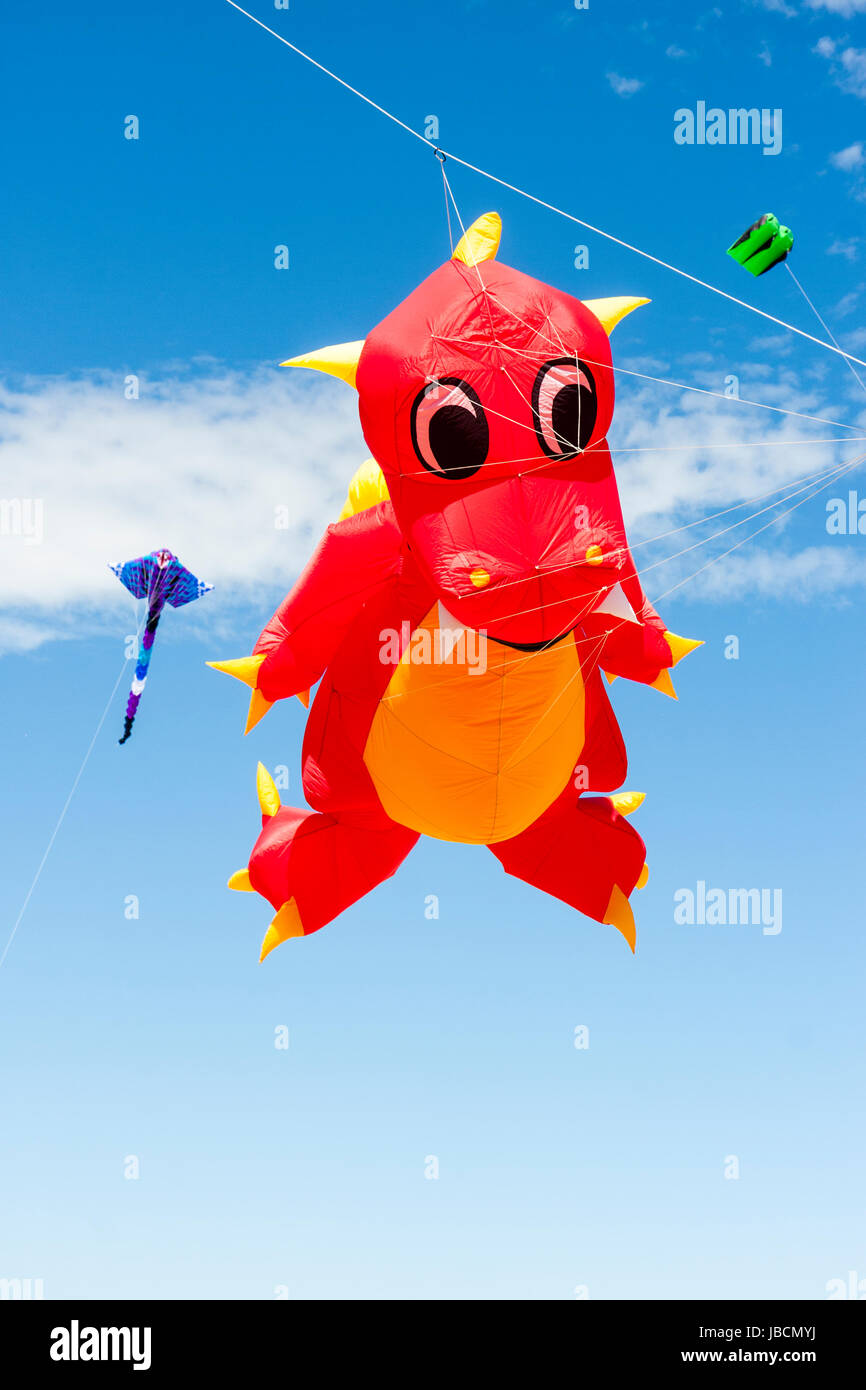 Red dragon kite flying in blue sky with other kites of various shapes ...