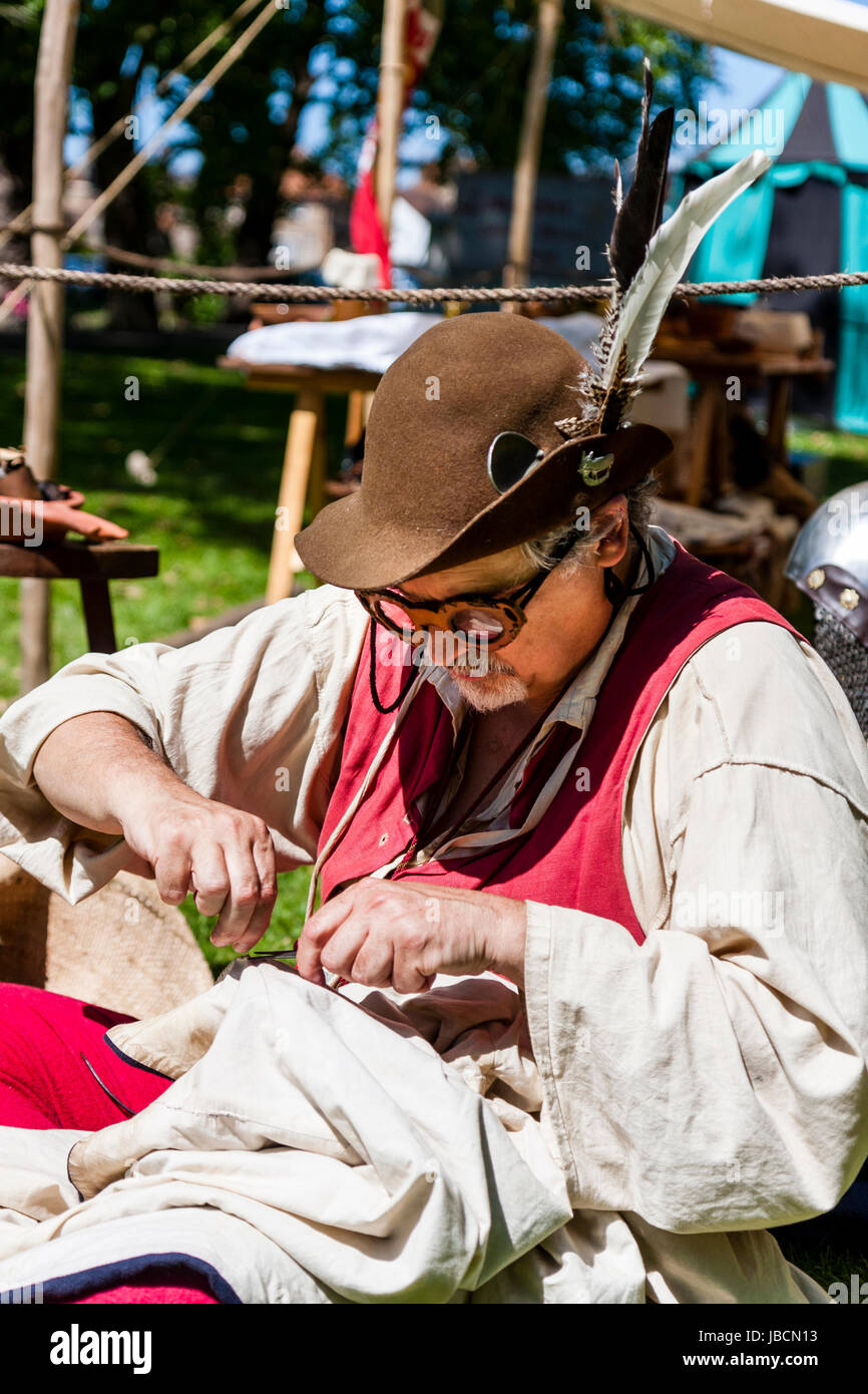 Re-enactment, Medieval weaver, with glasses, sitting on grass while ...