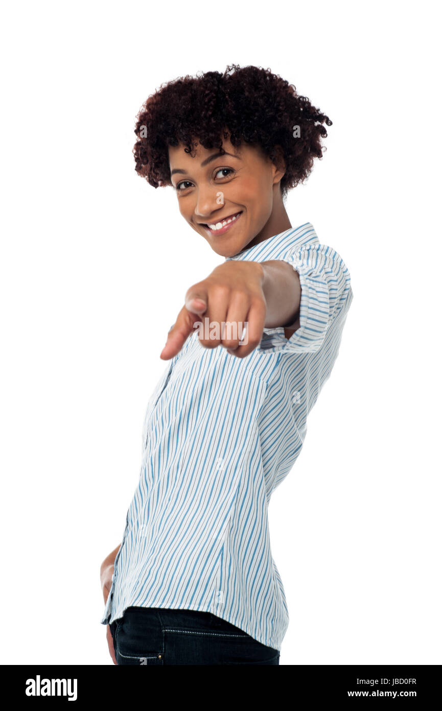 Joyous young lady standing sideways and pointing towards you, curly ...