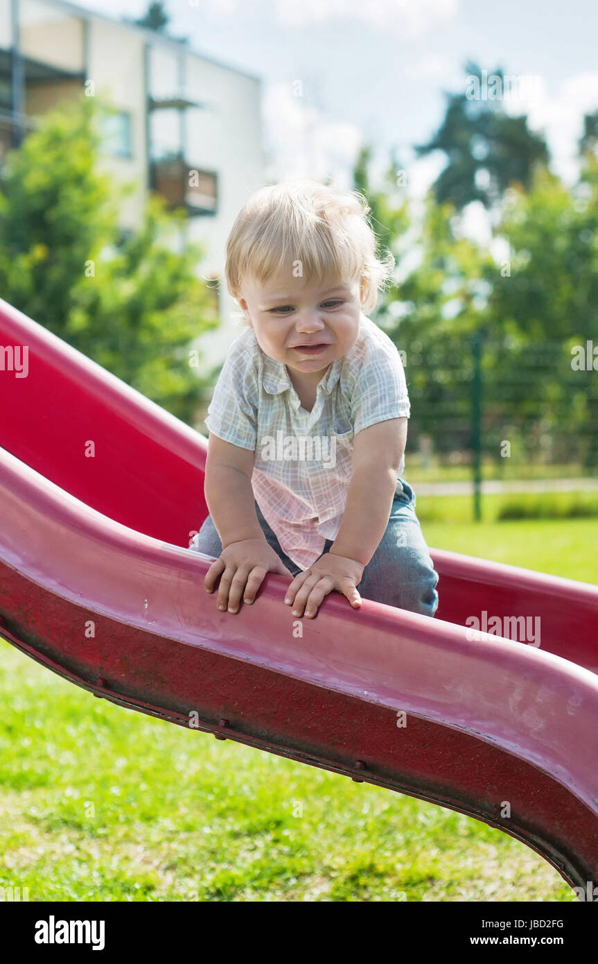 Baby boy on a red slide in playground Stock Photo - Alamy