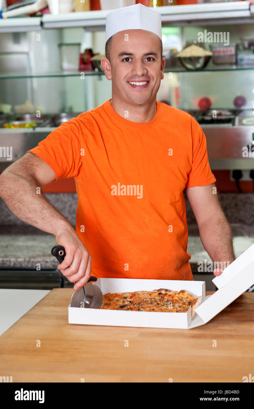 Handsome chef cutting hot pizza into pieces Stock Photo - Alamy