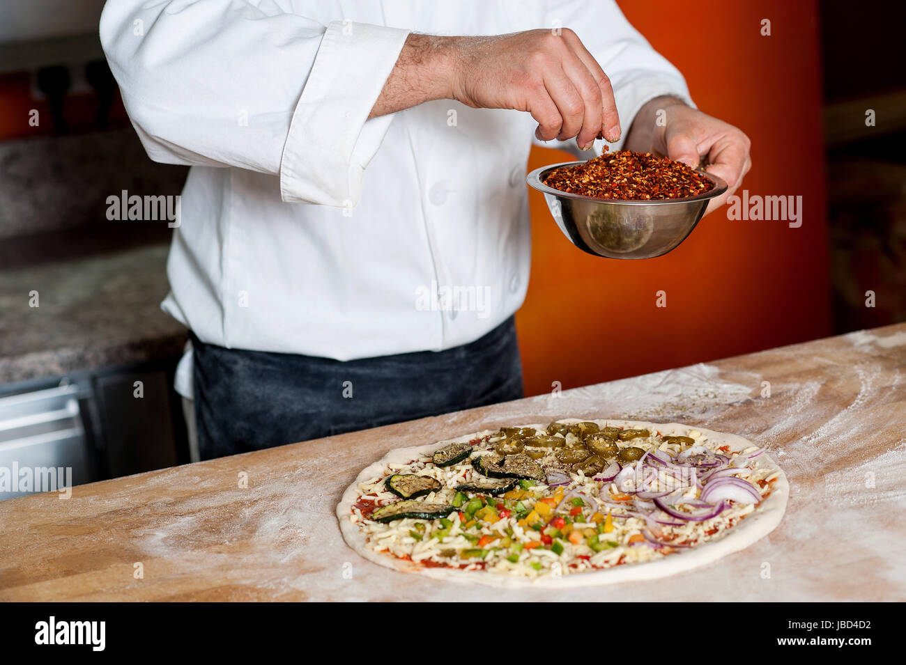 Male chef sprinkling chilli flakes over pizza Stock Photo - Alamy