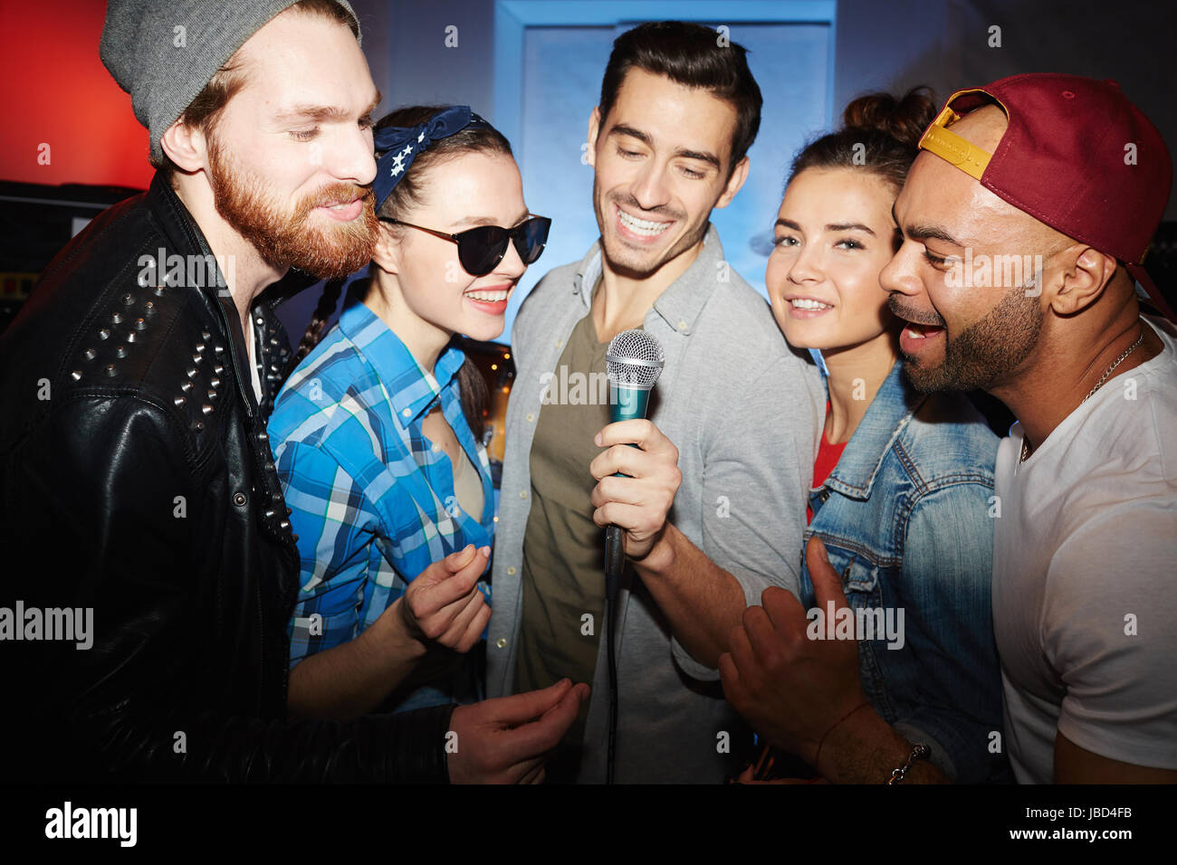 Group of smiling party people, men and women, standing on stage singing ...