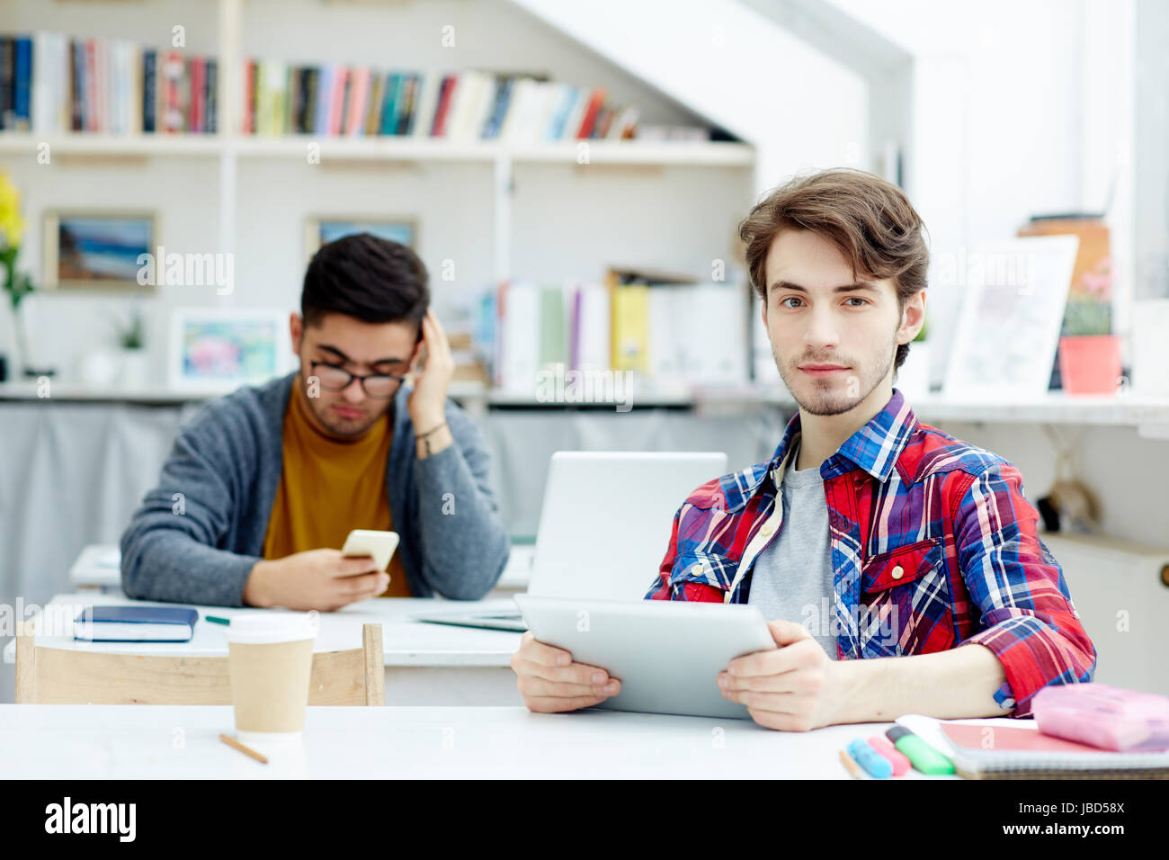 Adolescent man with touchpad sitting by desk in design studio or ...