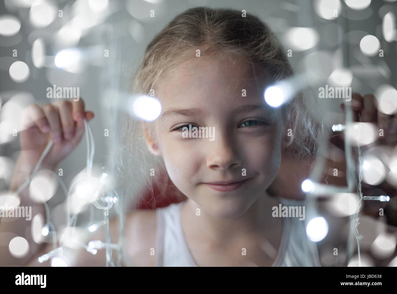 Portrait of a cute preschool girl with a radiant garland of lights in ...
