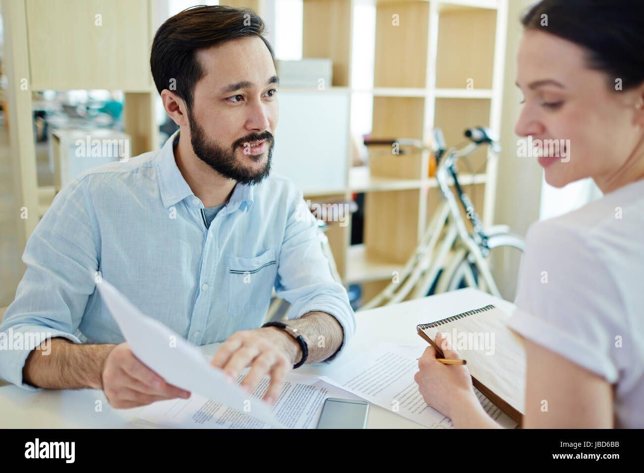 Two young co-workers discussing business papers at meeting Stock Photo ...