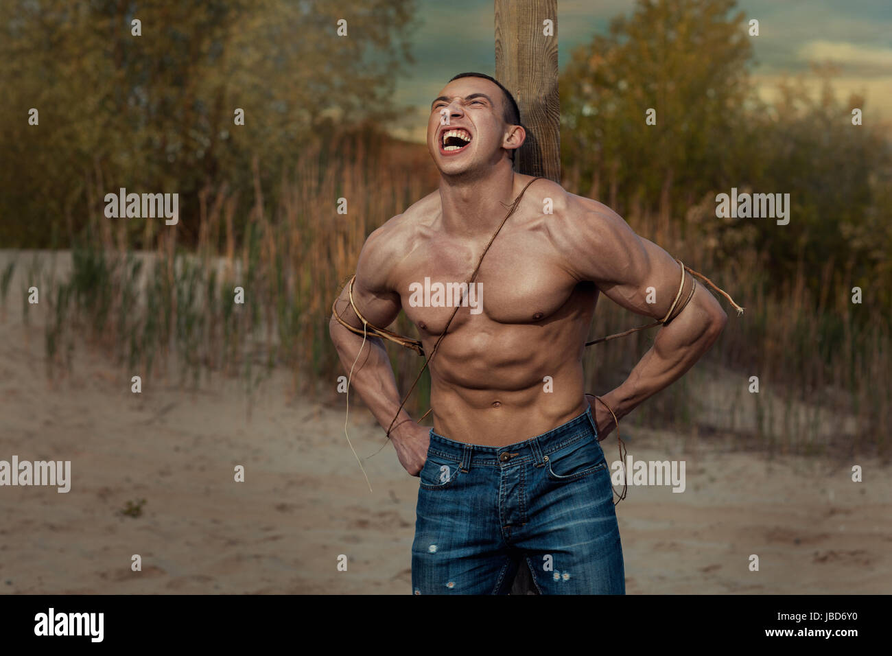Man with large muscles screaming. He is tied to a pole Stock Photo - Alamy