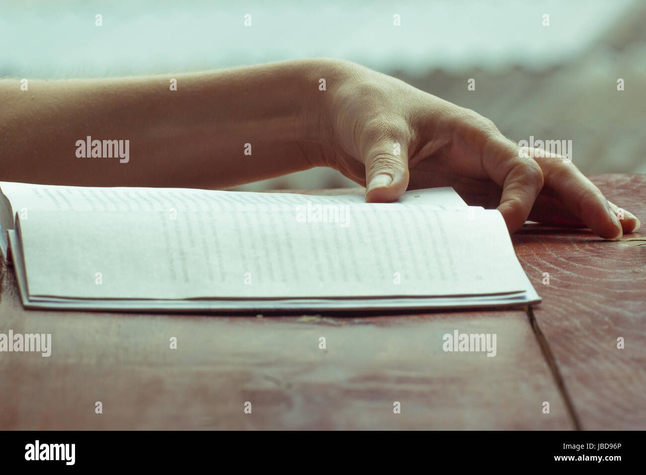 woman hand hold a pages in a book. reading a book on a table. side view ...