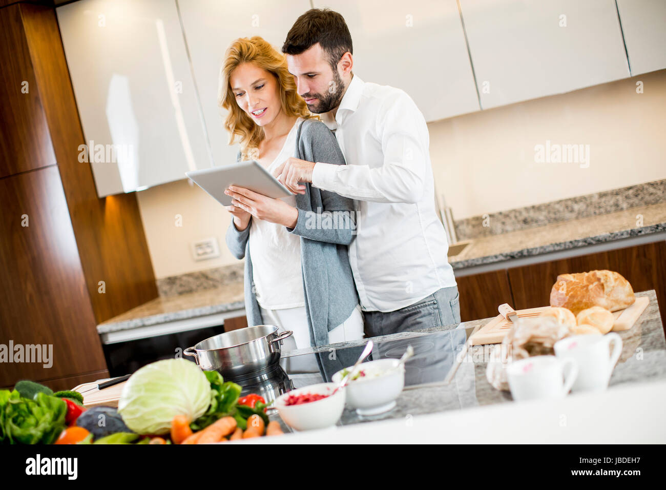 View at young man helping his girlfriend cooking in modern kitchen ...