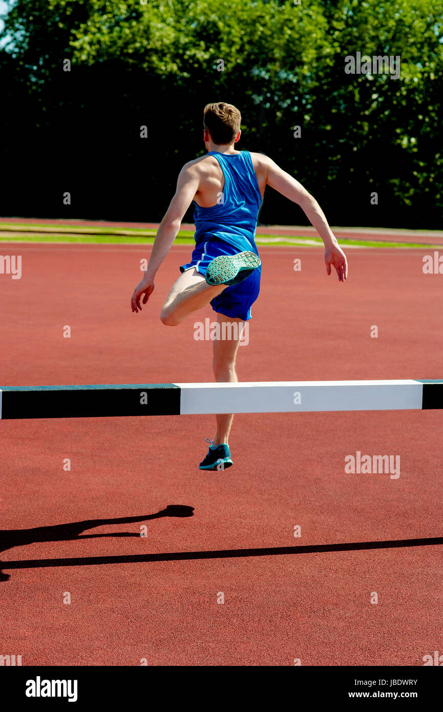 Back view of male athlete after crossing hurdle Stock Photo - Alamy
