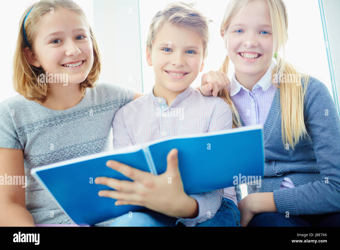 Portrait of three happy classmates with exercise book looking at camera ...