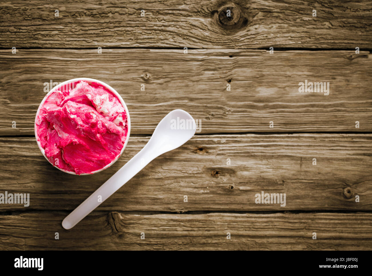 Appetizing tub of bright pink berry ice cream on a rustic wooden table ...