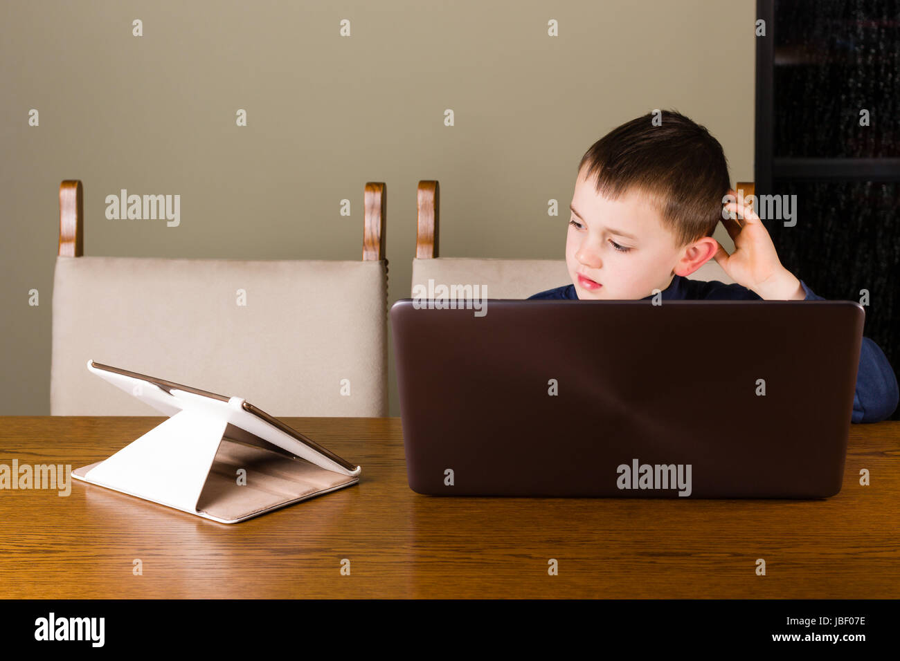 Cute little boy on new technology, sitting behind a laptop and tablet ...