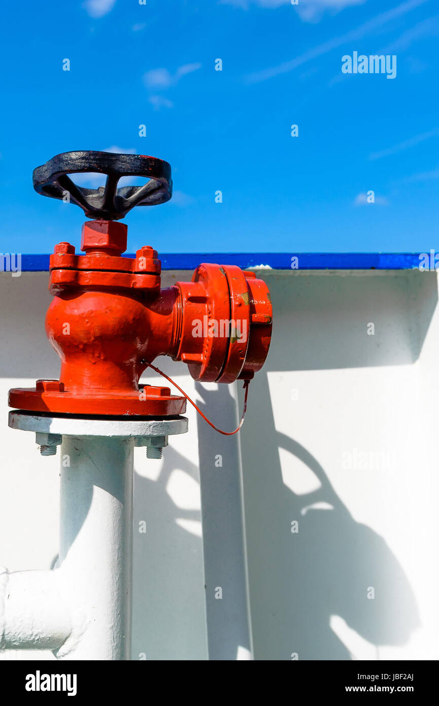 Red water or fuel valve against white wall and blue sky background ...