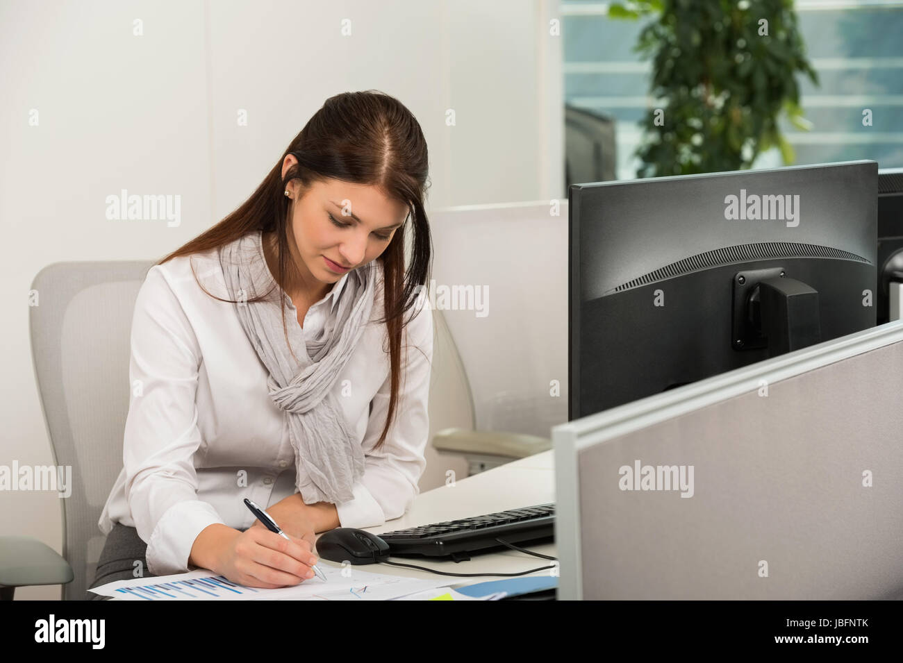 Businesswoman sitting while writing at computer desk Stock Photo - Alamy
