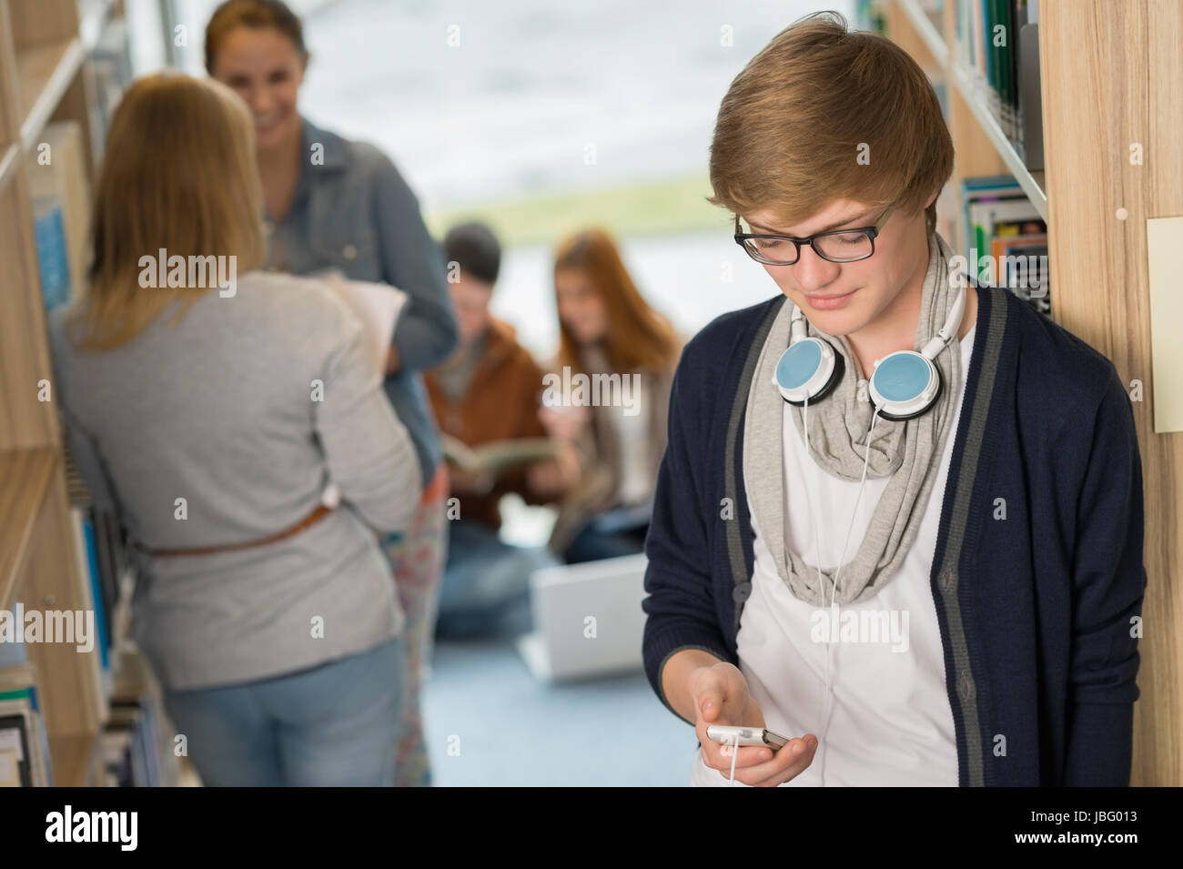 Student with headphones using mobilephone with friends in library Stock ...