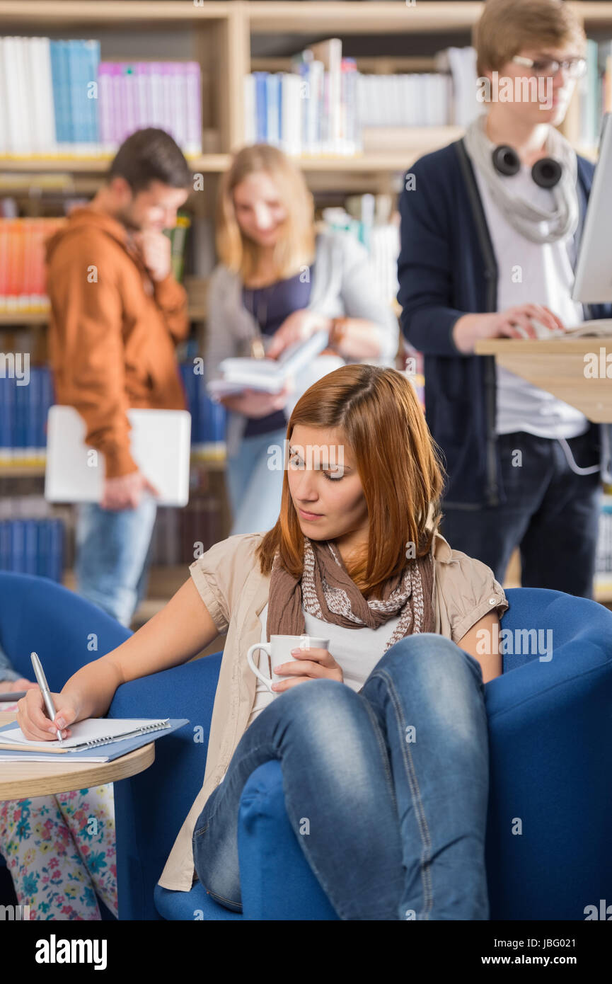 Young student writing notes with friends in background at library Stock ...