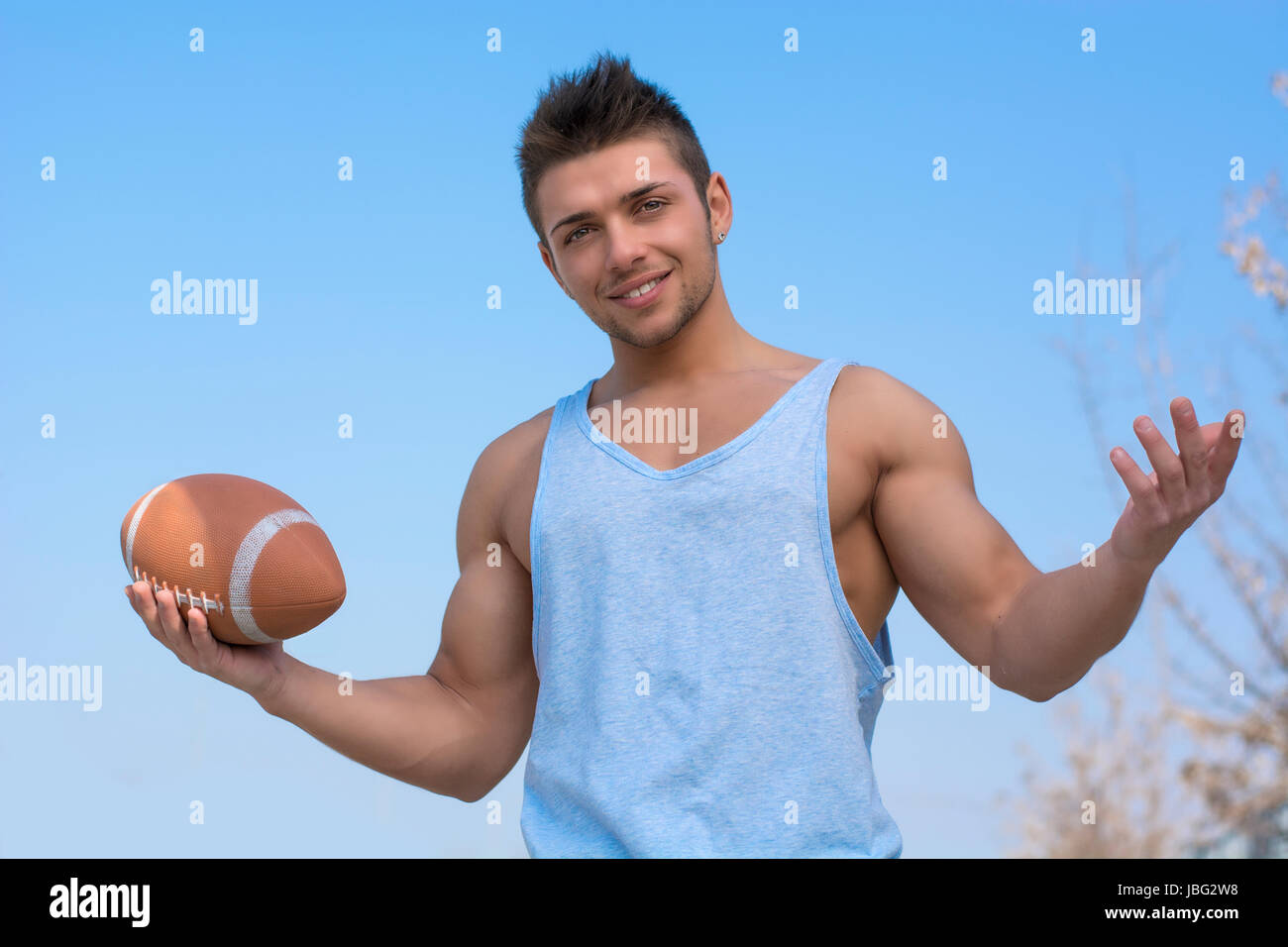 Muscular american football player standing with ball in hand, arms open ...
