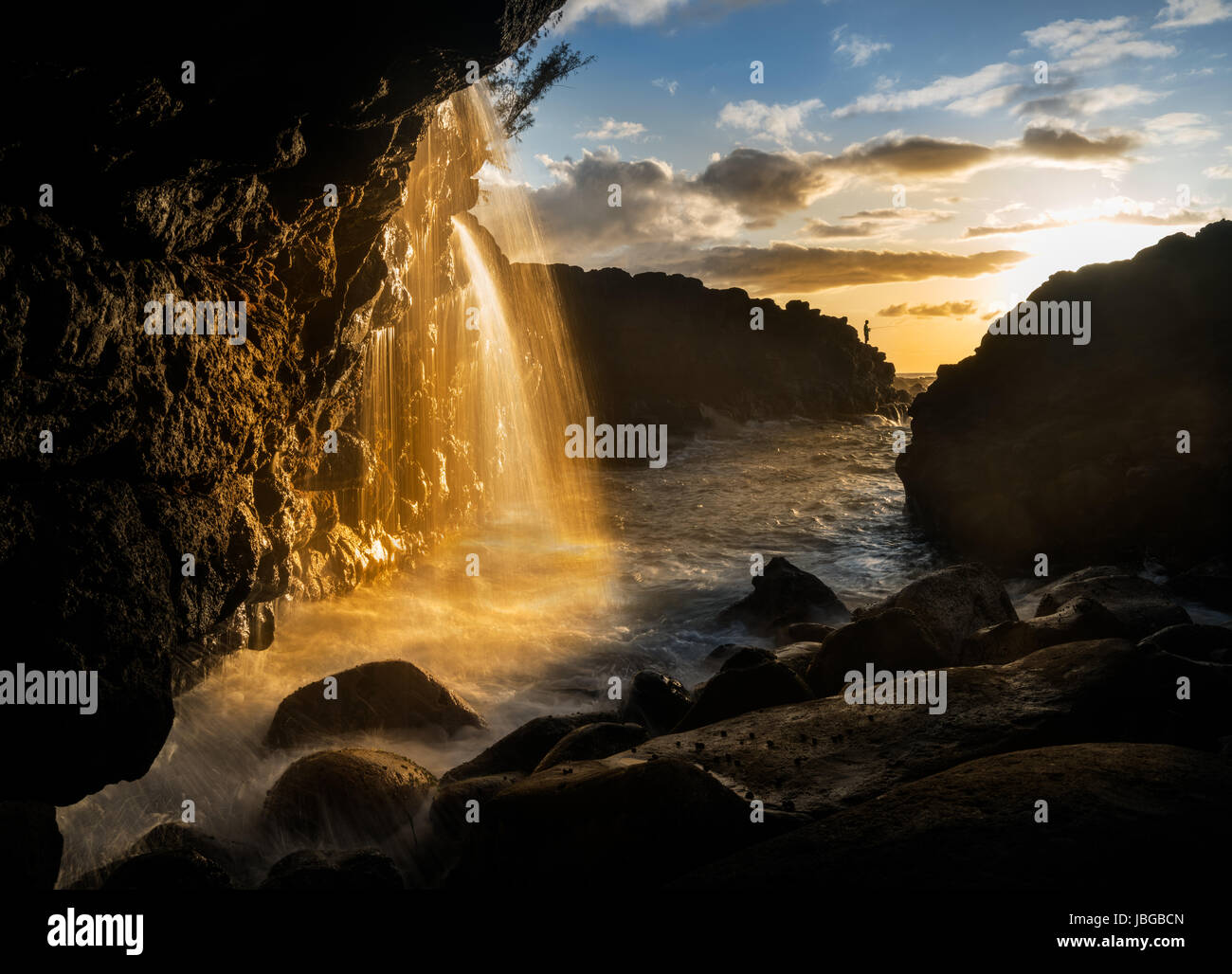 Setting sun at sunset illuminates a small waterfall falling into the ...